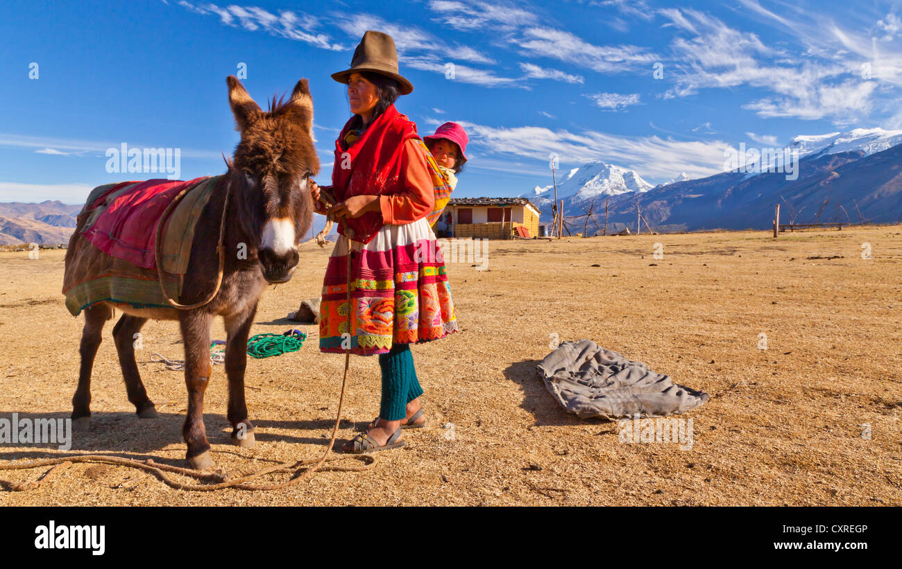 Woman wearing a red traditional dress carrying a baby, with a donkey ...