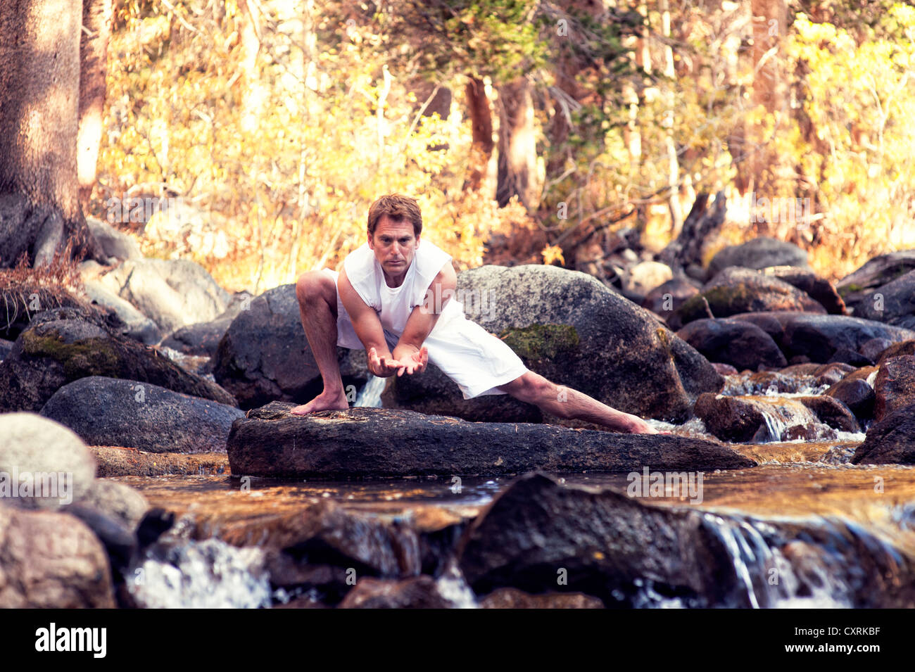Man in a deep yoga pose in a wooded river Stock Photo - Alamy