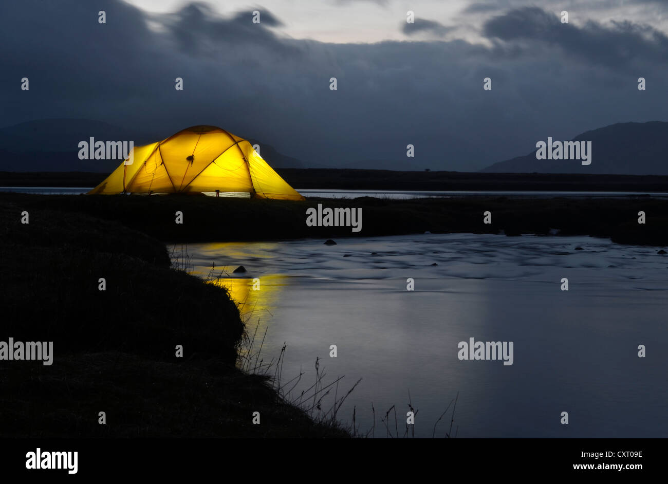 Yellow illuminated expedition tent, trekking tent, on a river estuary ...