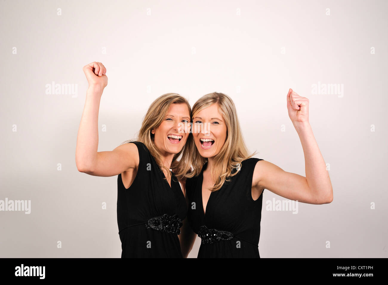 Twin sisters cheering with arms raised Stock Photo - Alamy