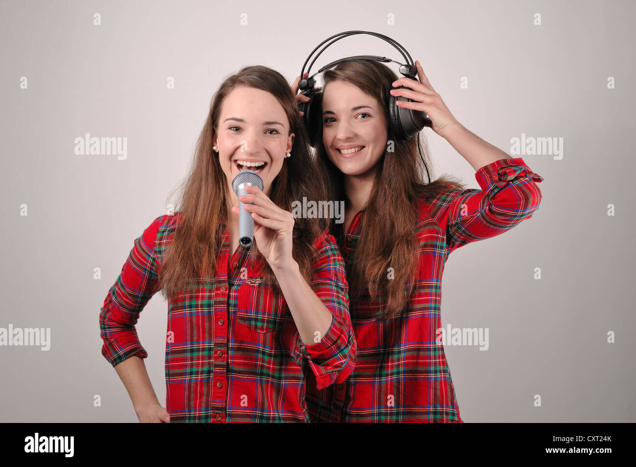 Twin sisters, one singing into a microphone, while the other listens ...