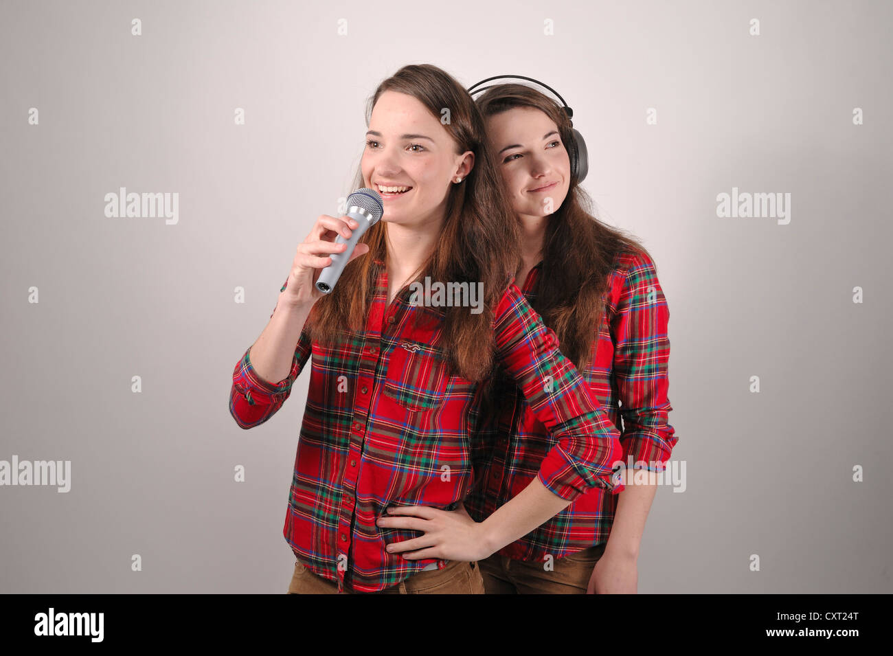 Twin sisters, one singing into a microphone, while the other listens ...
