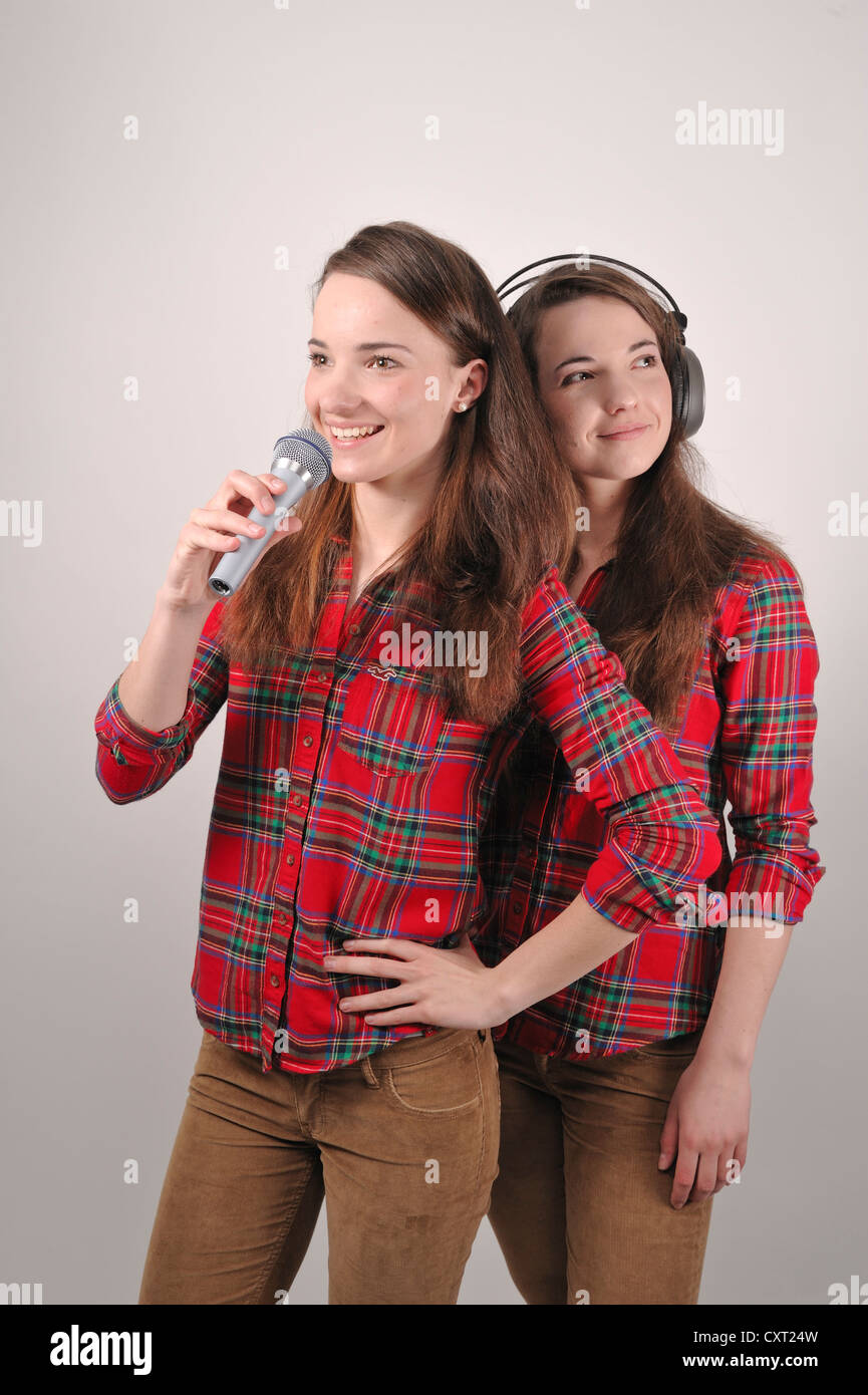 Twin sisters, one singing into a microphone, while the other listens ...