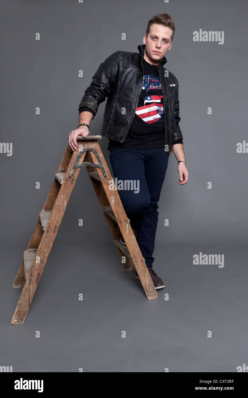 Young man wearing a leather jacket and jeans, standing next to an old ...