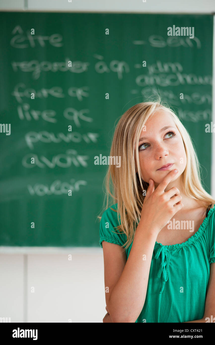Schoolgirl standing in front of a blackboard in a classroom, looking ...
