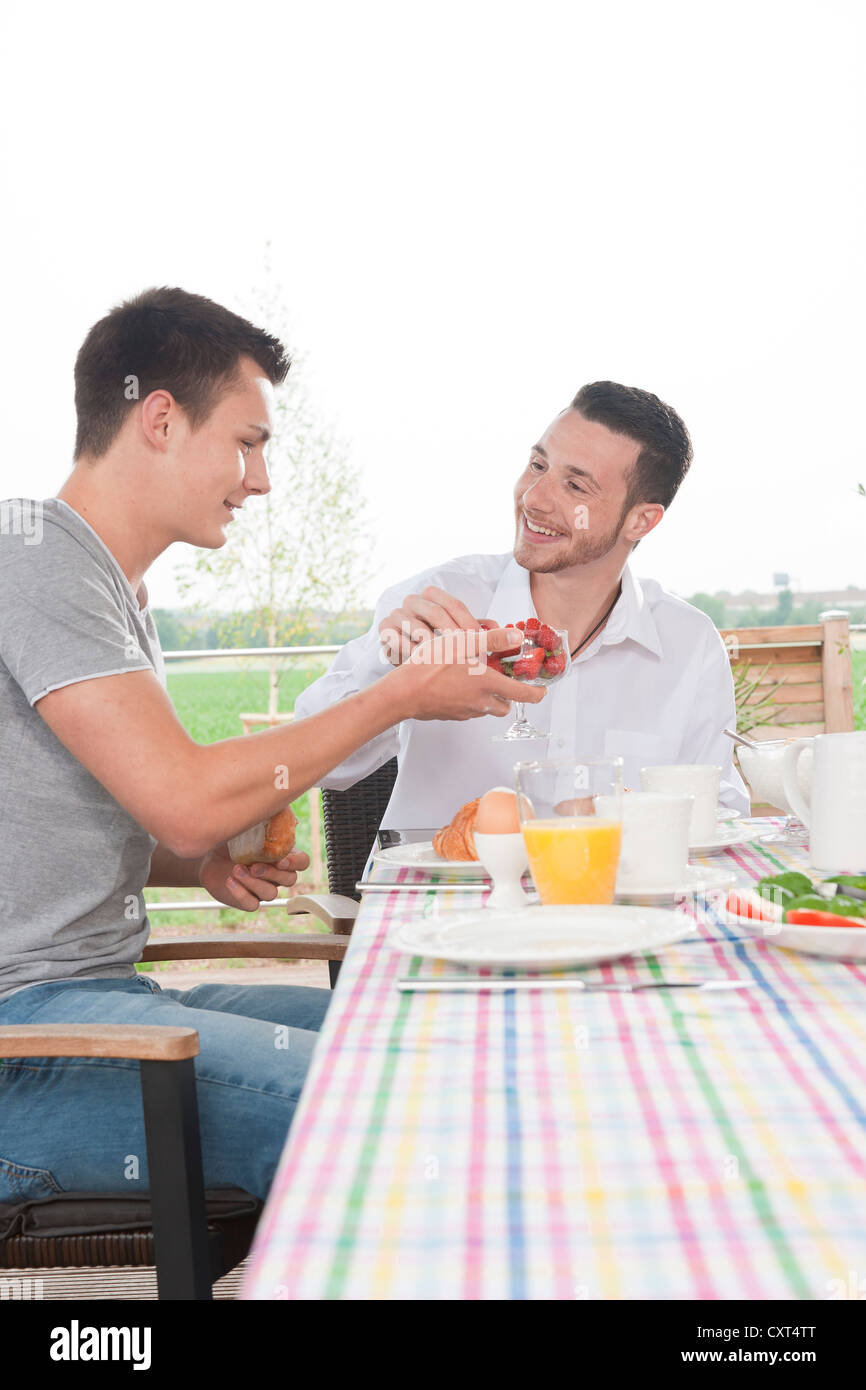 Two young men having breakfast on a terrace Stock Photo - Alamy