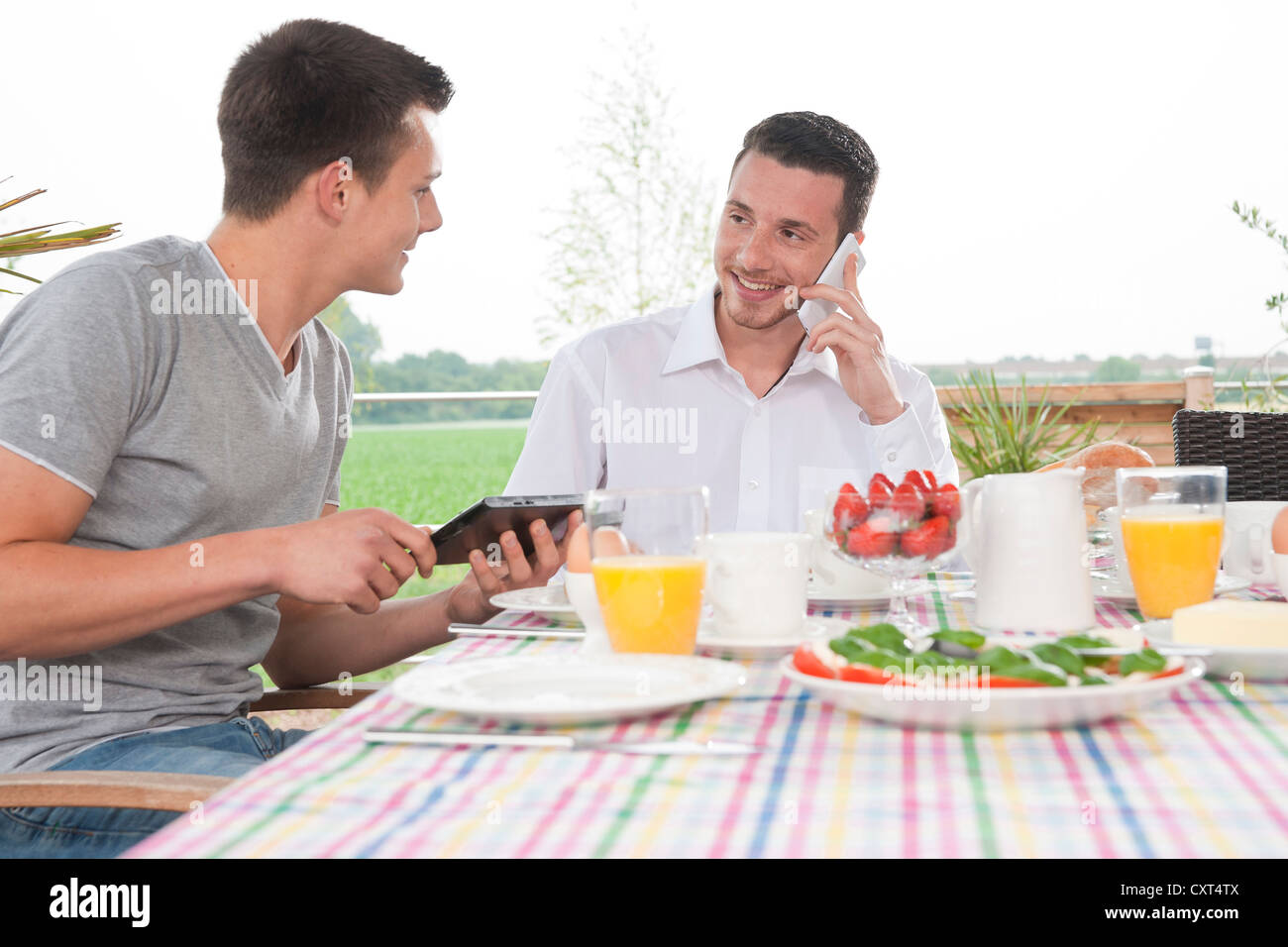 Two young men having breakfast on a terrace Stock Photo - Alamy