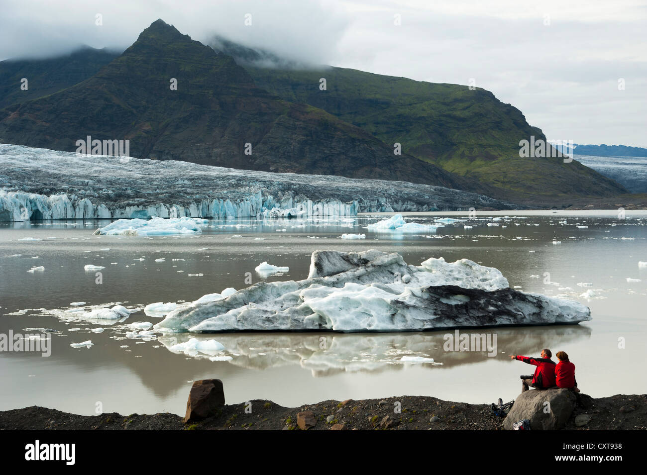 A pair observing black ash-coloured icebergs and a glacier tongue ...