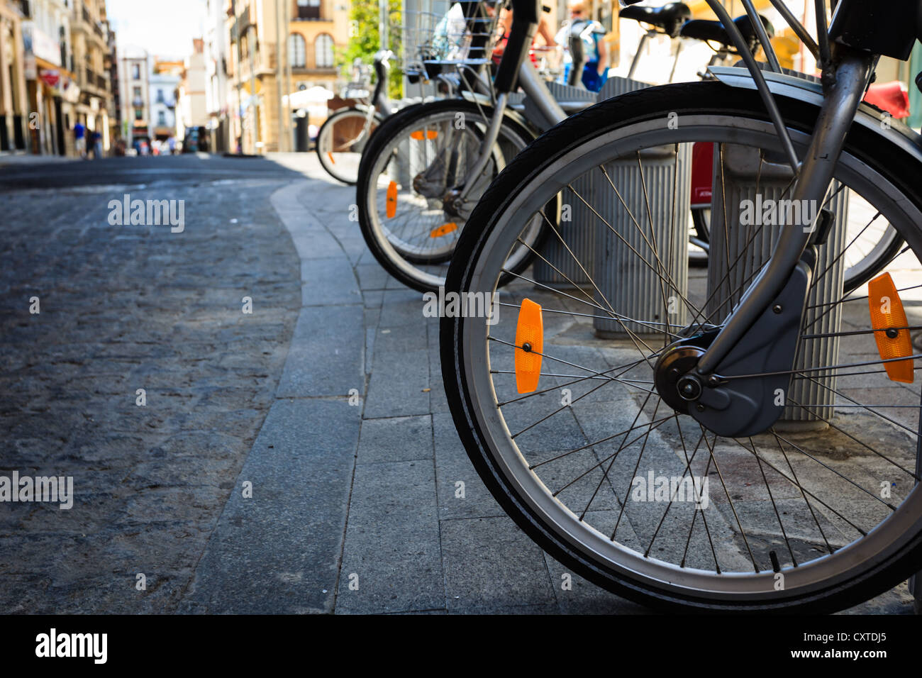 Row of modern bike front tires border old cobblestone street in Seville ...