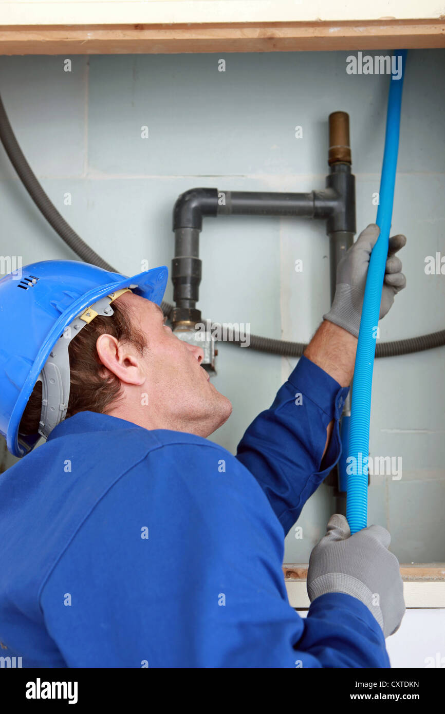 Plumber feeding blue pipe behind a false wall Stock Photo - Alamy
