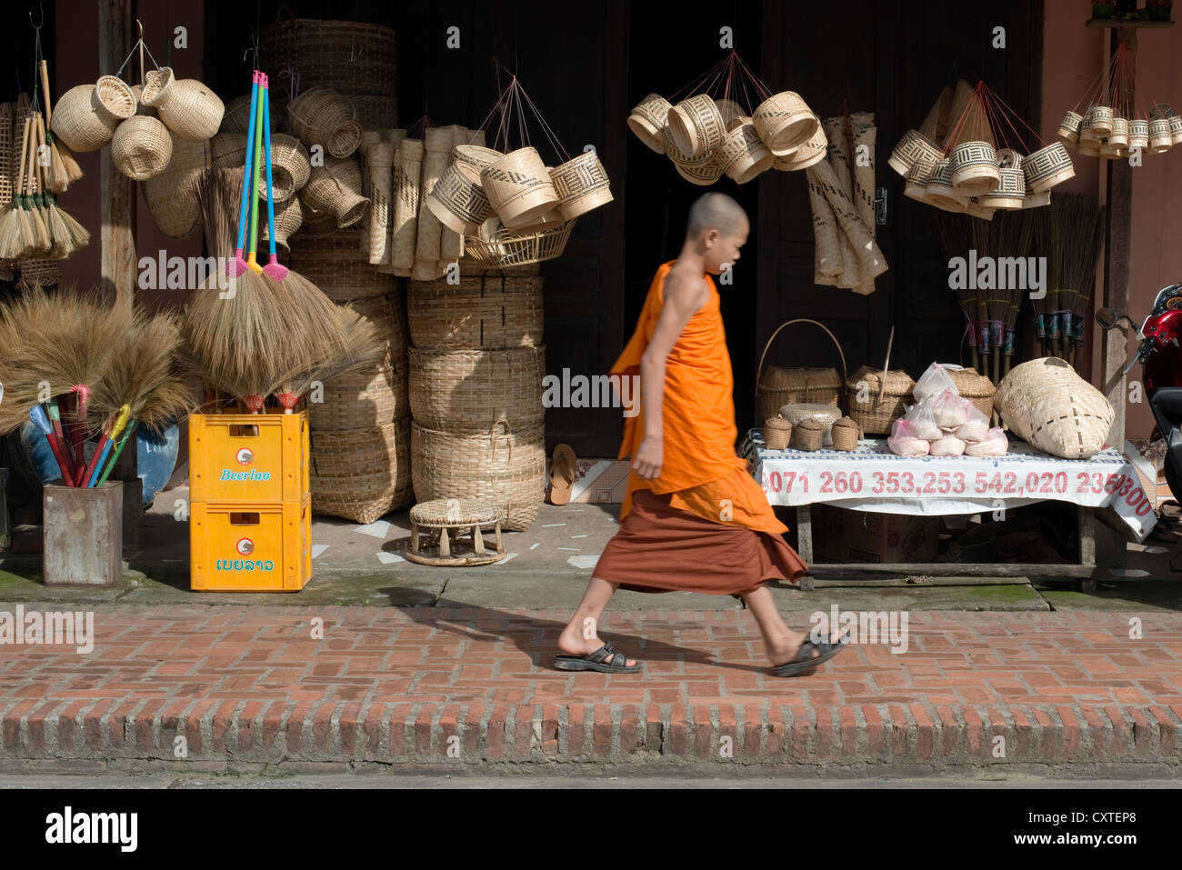 A young monk walks past a shop selling baskets in Luang Prabang, Laos ...