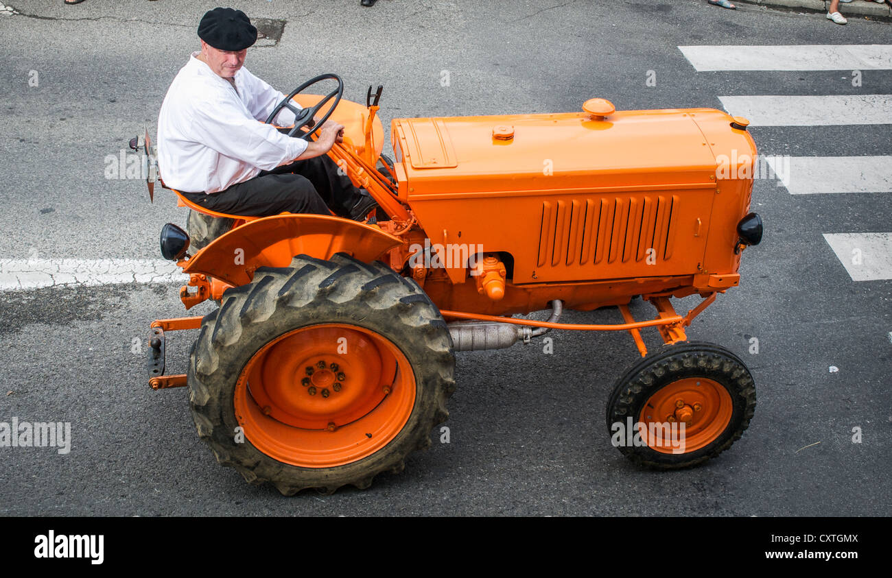 An unidentified man with a beret driving an orange French tractor in ...