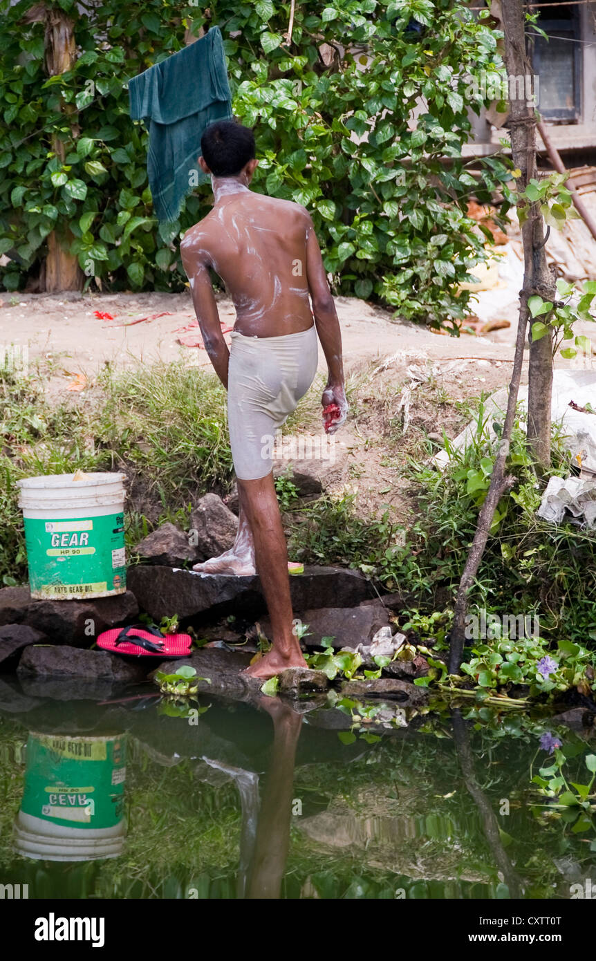 Vertical portrait of a man washing himself by the side of the river in ...