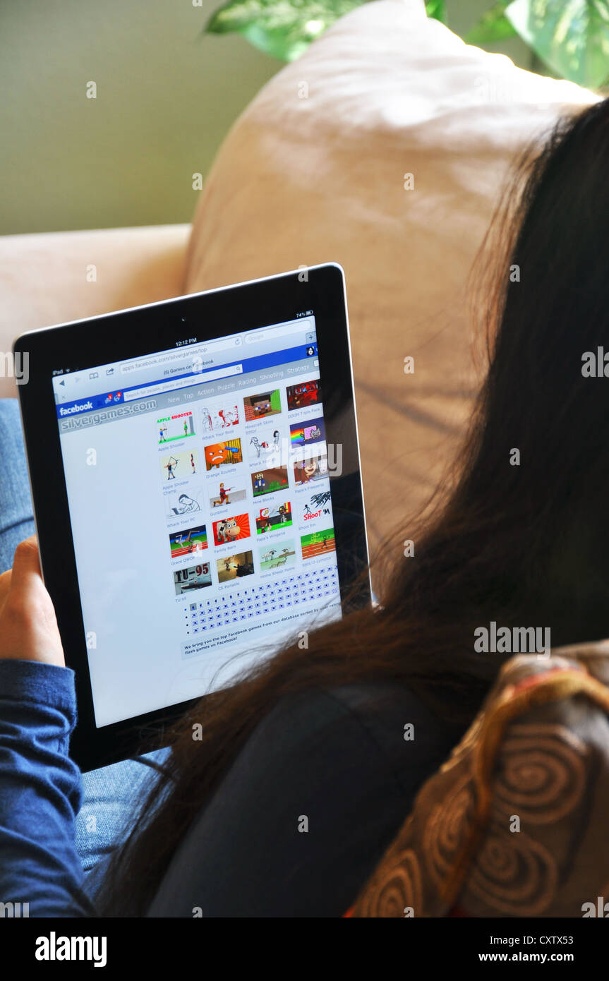 Young girl with iPad sitting on sofa at home. Silvergames website shown ...