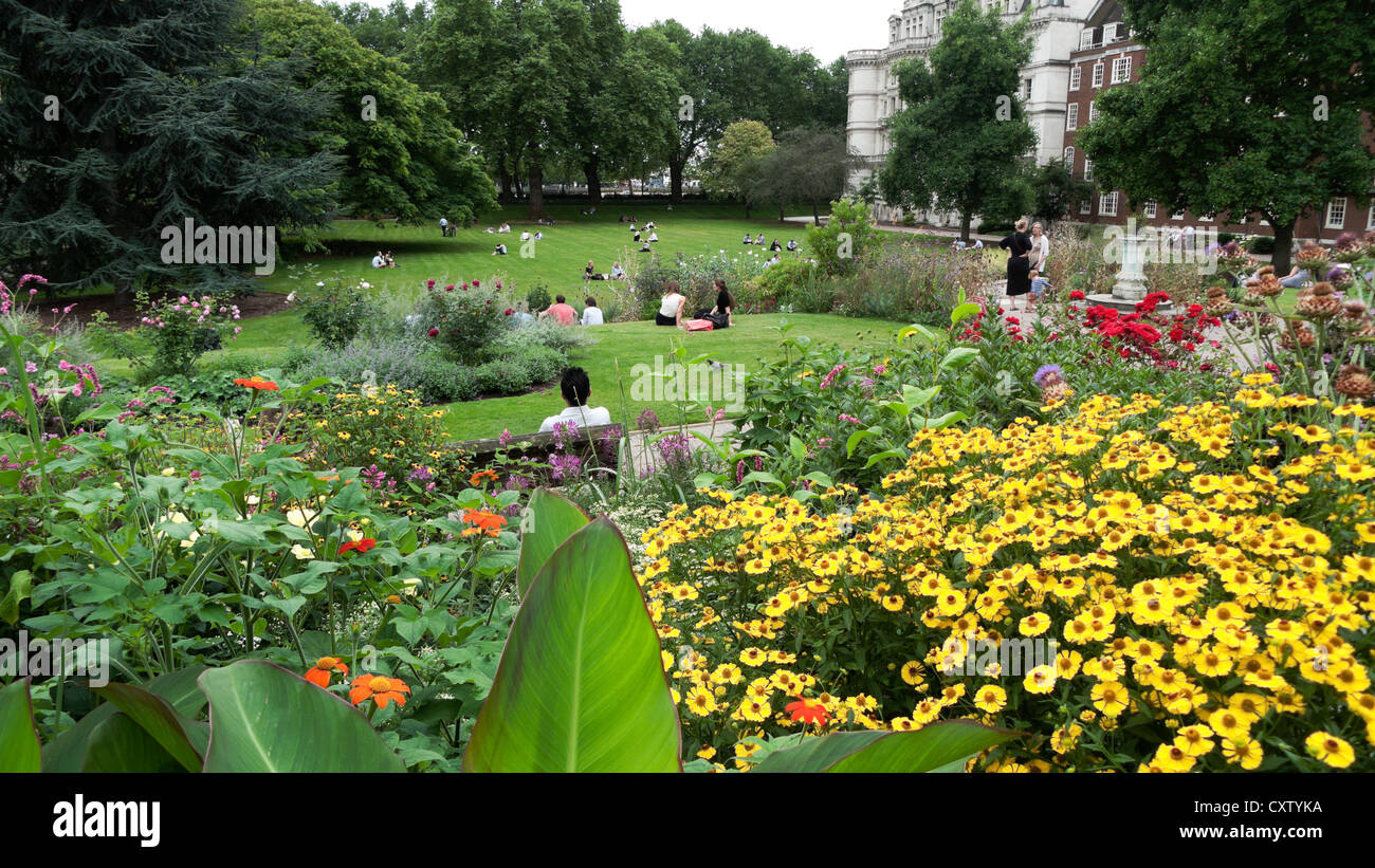 People relaxing in the Inner Temple Gardens by the flower beds with yellow flowers and canna ...