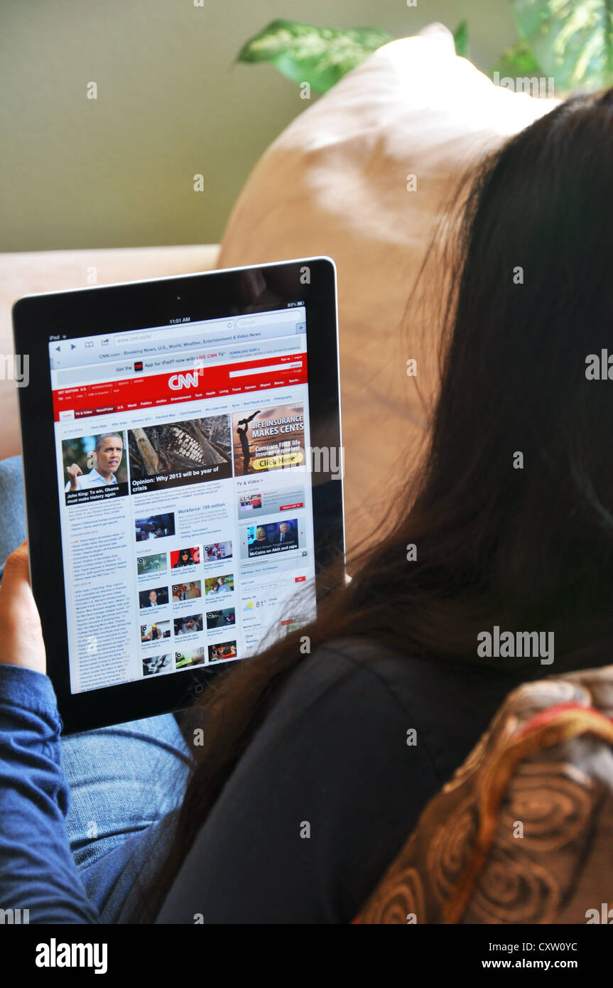Young girl with iPad sitting on sofa at home. CNN news website shown on the iPad screen Stock ...