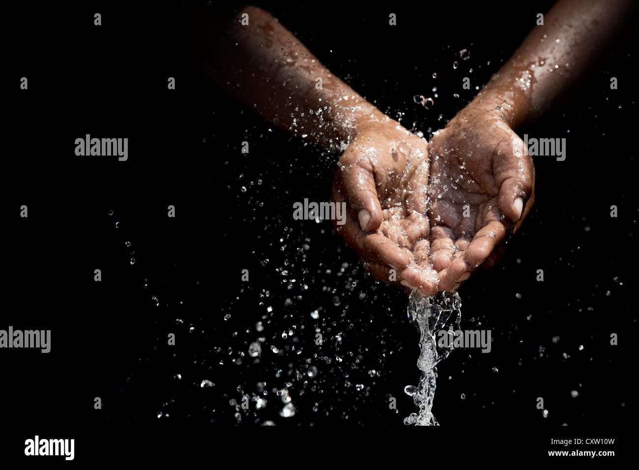 Indian mans cupped hands catching poured water against black background ...