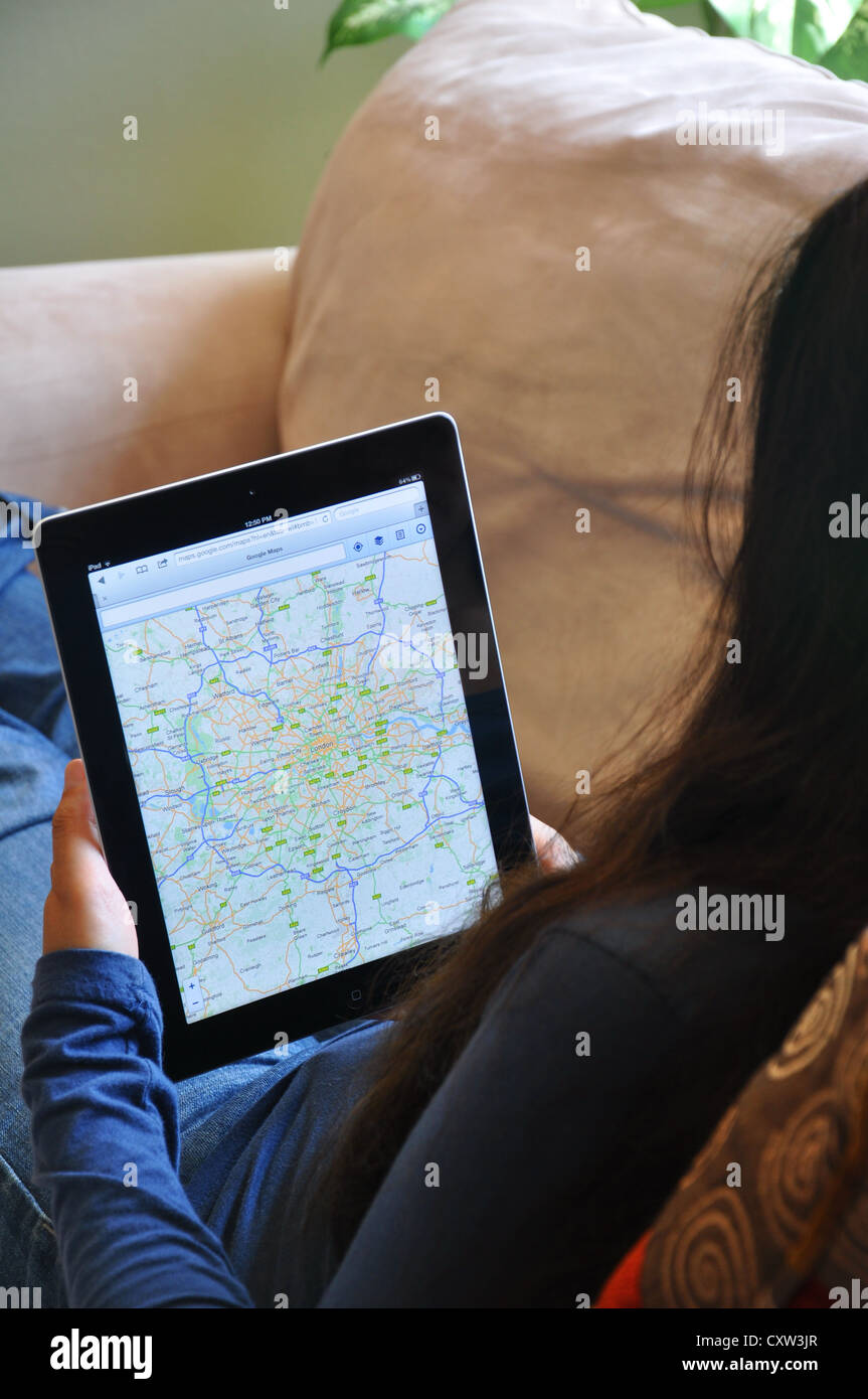 Young girl with iPad sitting on sofa at home. London map website shown ...