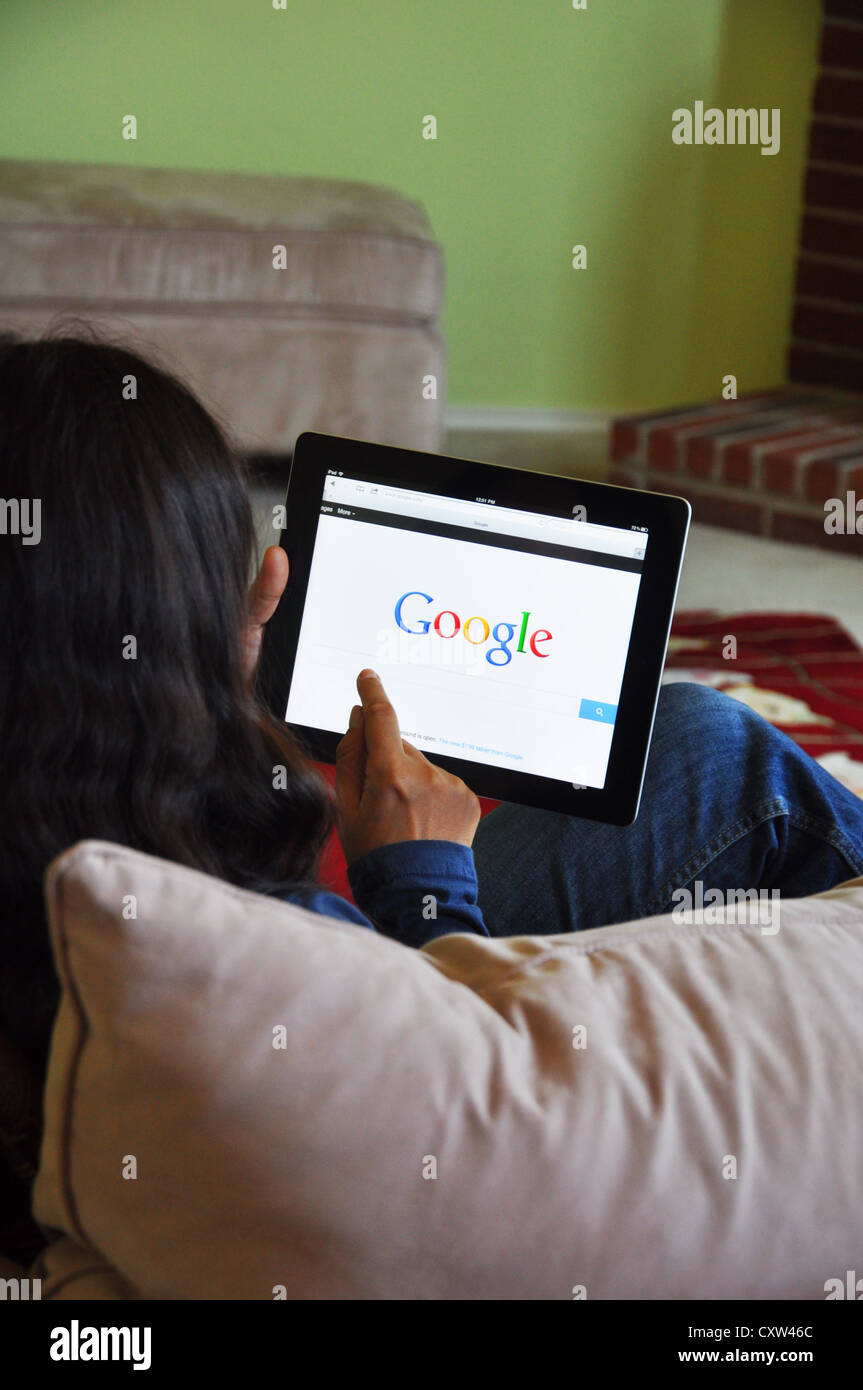 Young girl with iPad sitting on sofa at home. Google website shown on ...