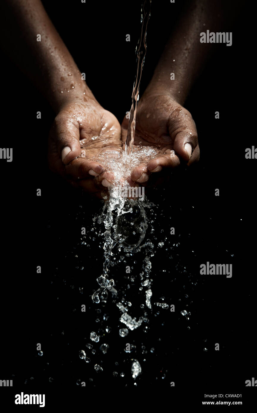 Indian mans cupped hands catching poured water against black background ...