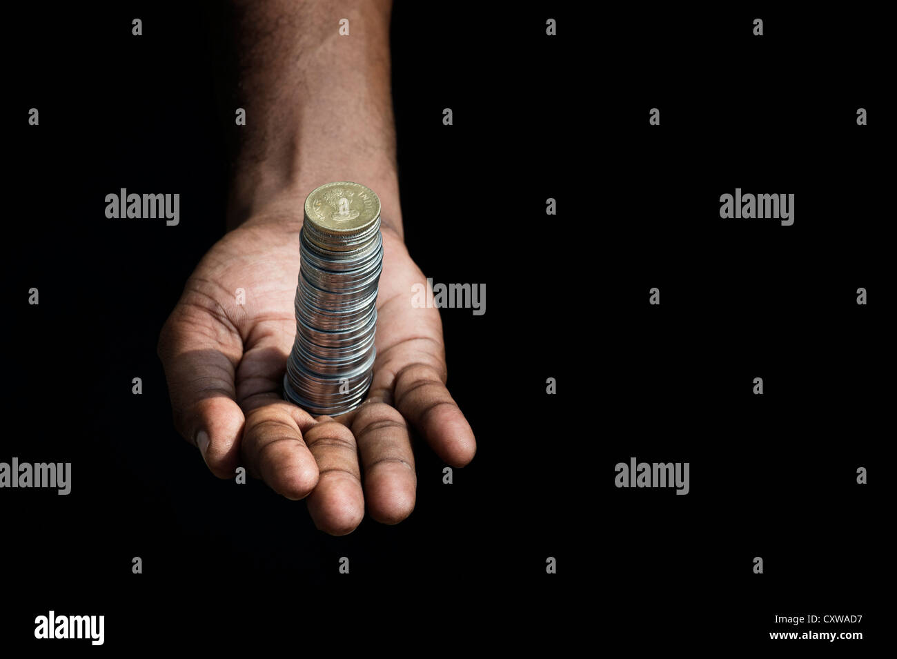 Indian mans hand with a stack of rupee coins against a black background ...