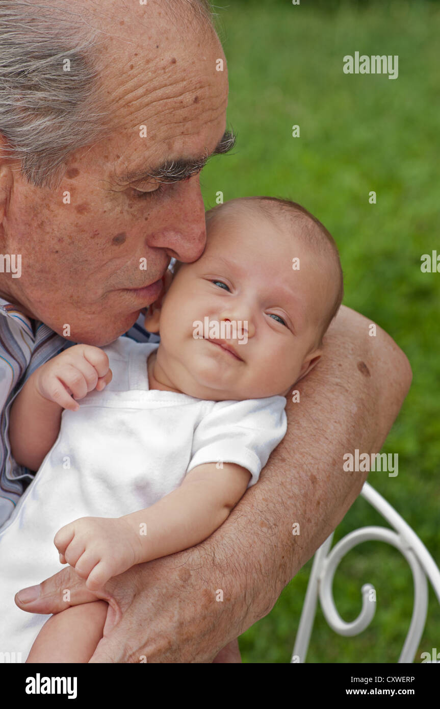 Senior man sitting on a chair in park is holding a baby boy in his ...