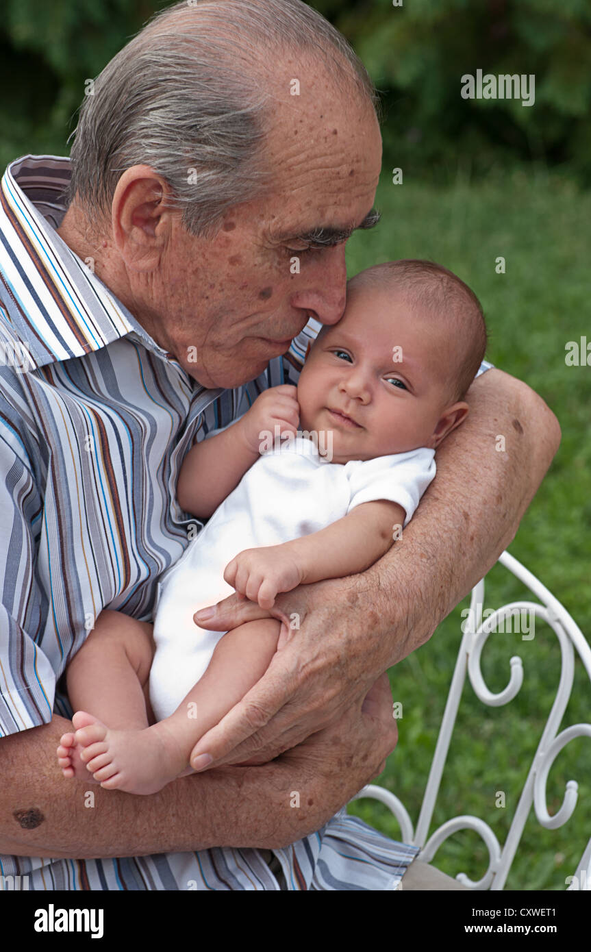 Senior man sitting on a chair in park is holding a baby boy in his ...
