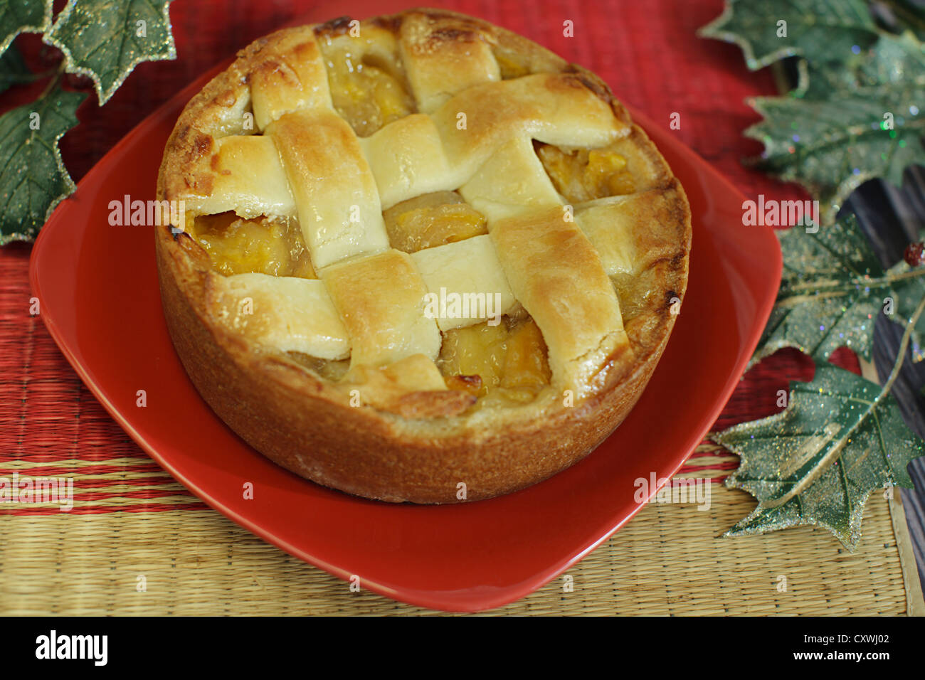 Deep dish torte with lattice crust on red plate. Christmas leaves and ...