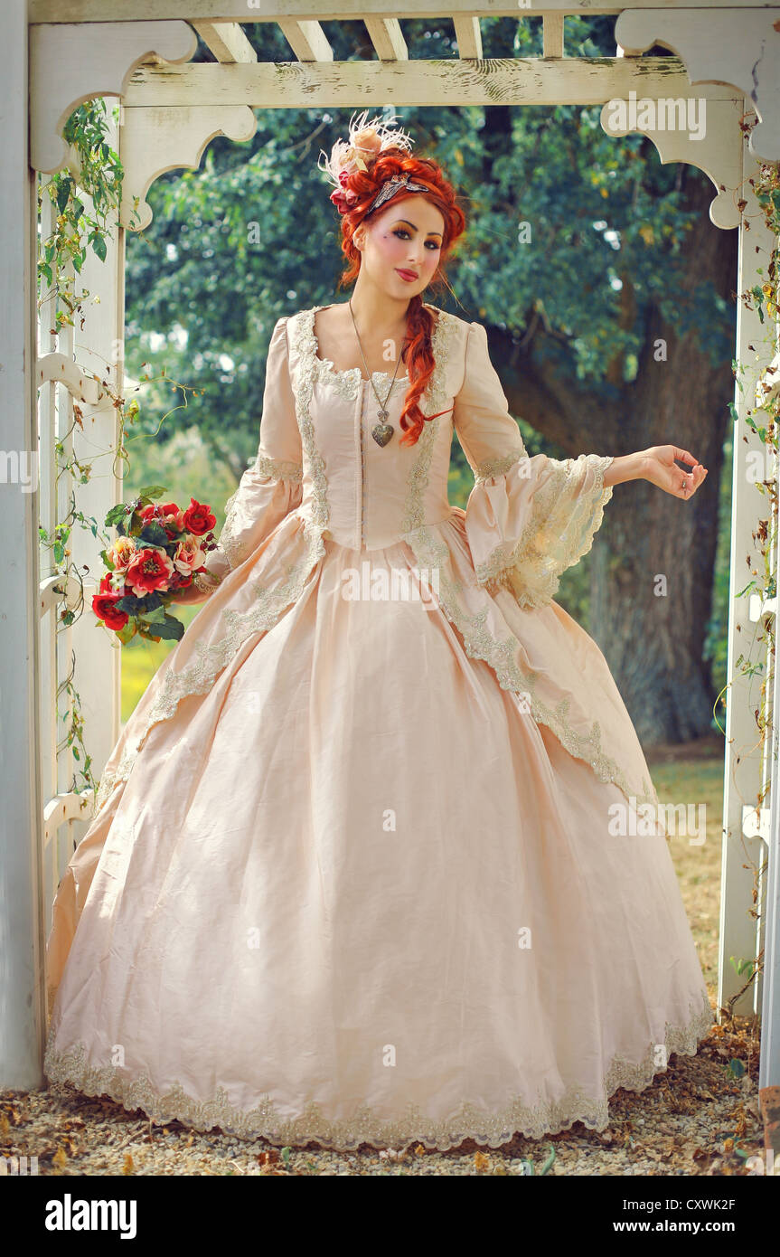 Young woman with long red hair in Regency period dress holding flowers ...