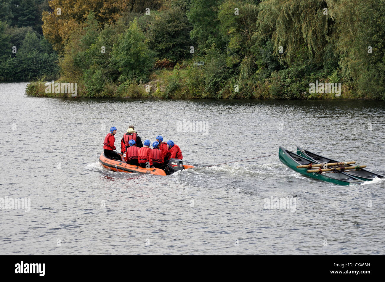 Orange rubber dinghy with full passenger load towing two lashed ...