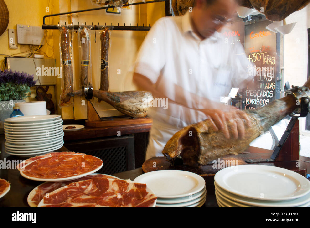 A man cutting slices of traditional Jamón Serrano in a tapas bar in ...
