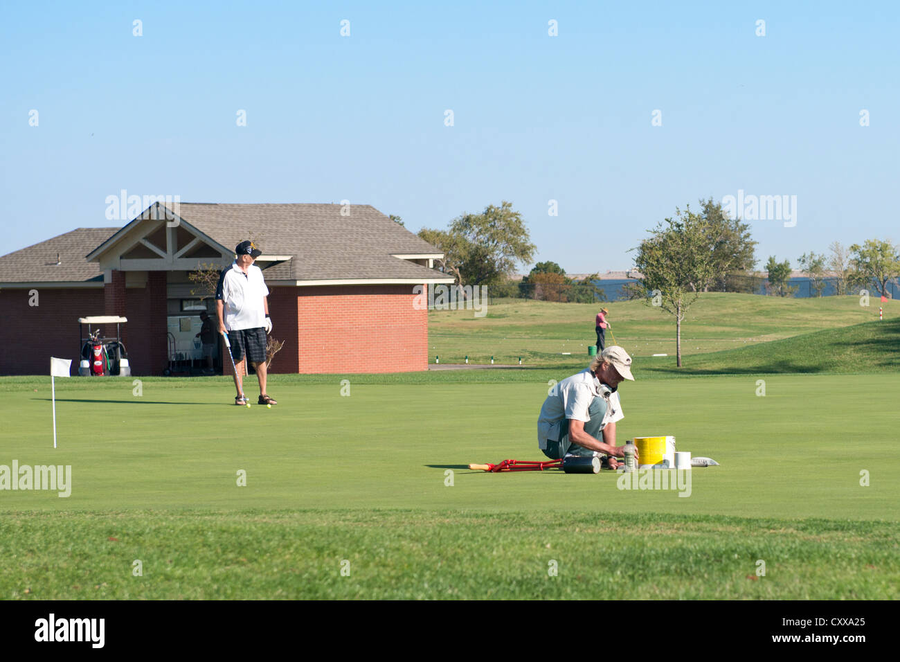 A groundskeeper prepares to make a new hole on a putting green at ...