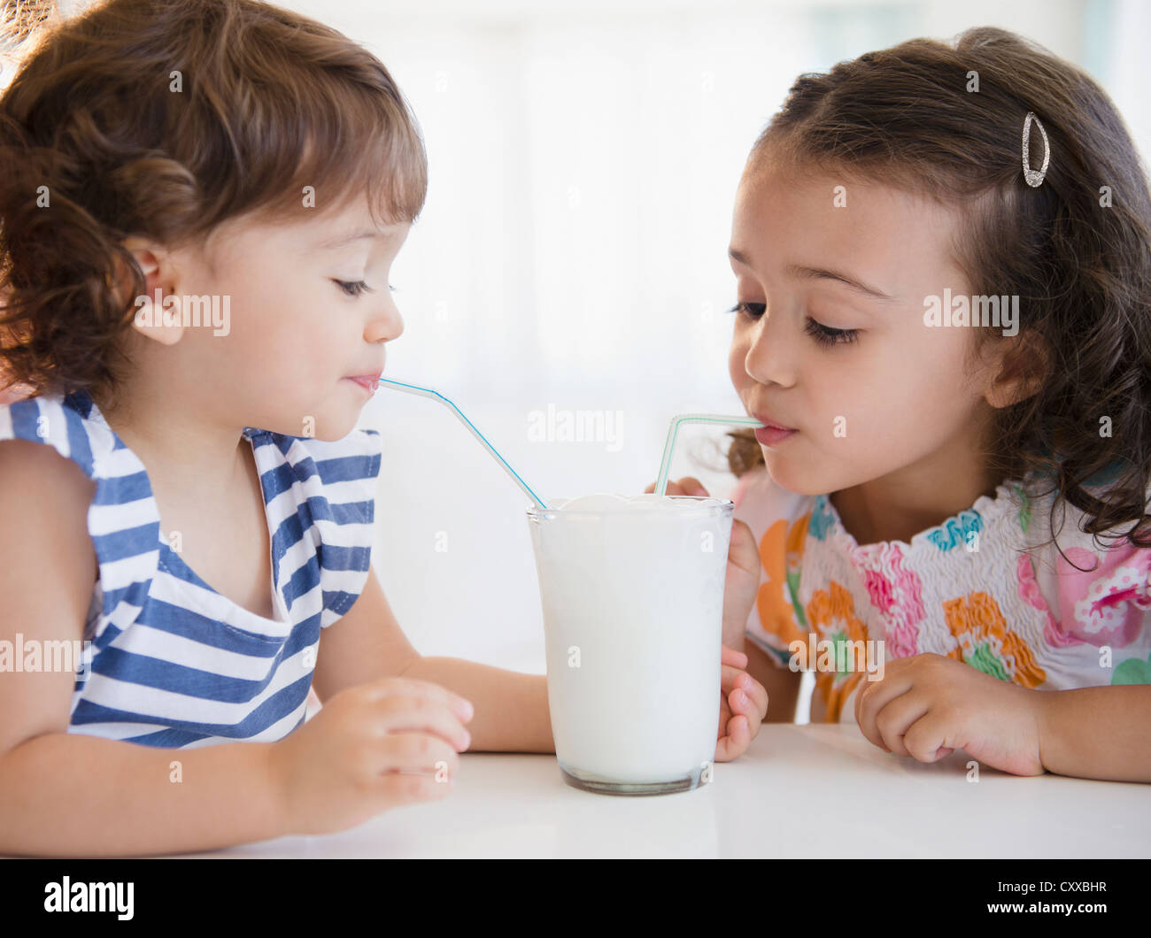 Mixed race sisters sharing glass of milk Stock Photo - Alamy