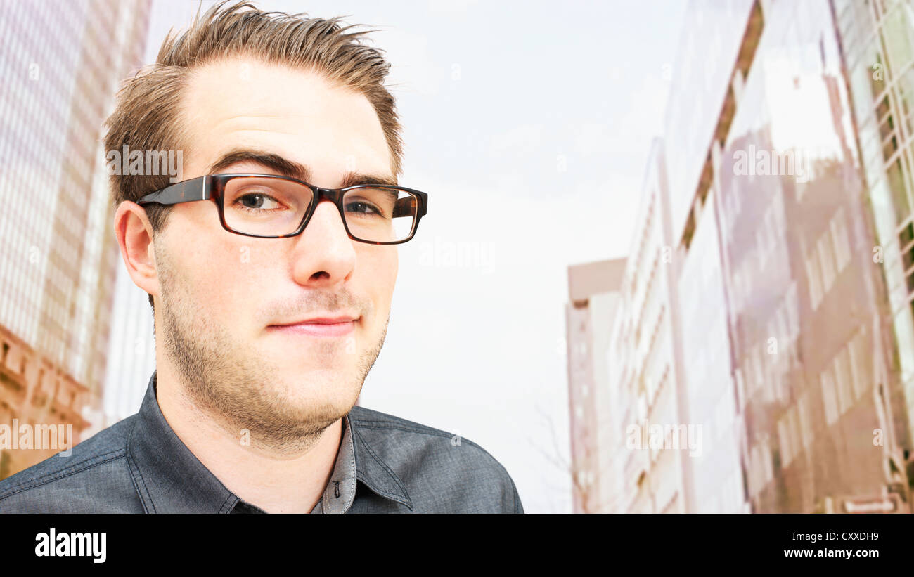 Portrait of a young man wearing glasses standing in front of high-rise ...
