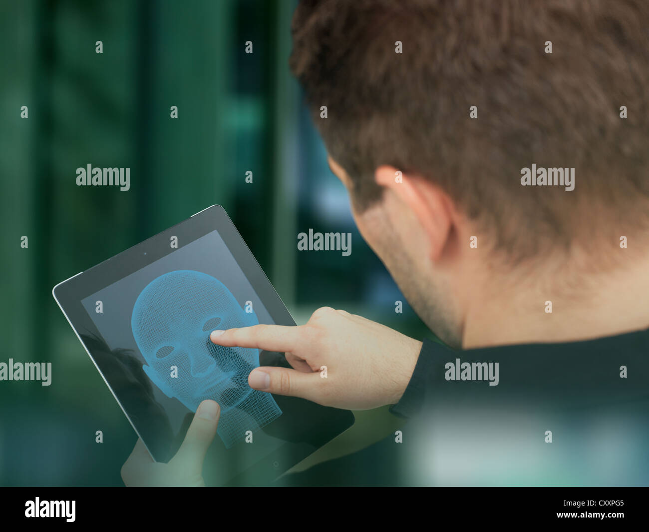 Young businessman touching an iPad with his finger, seen from behind ...