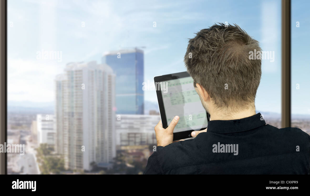 Young businessman working with an iPad in front of a window, a skyline ...