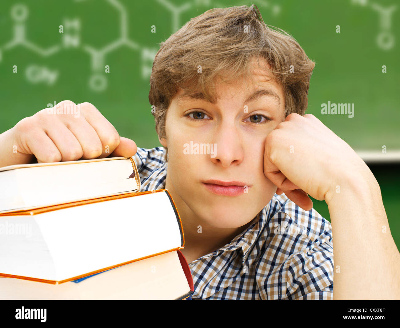 Overworked student sitting in front of a blackboard with a stacks of ...