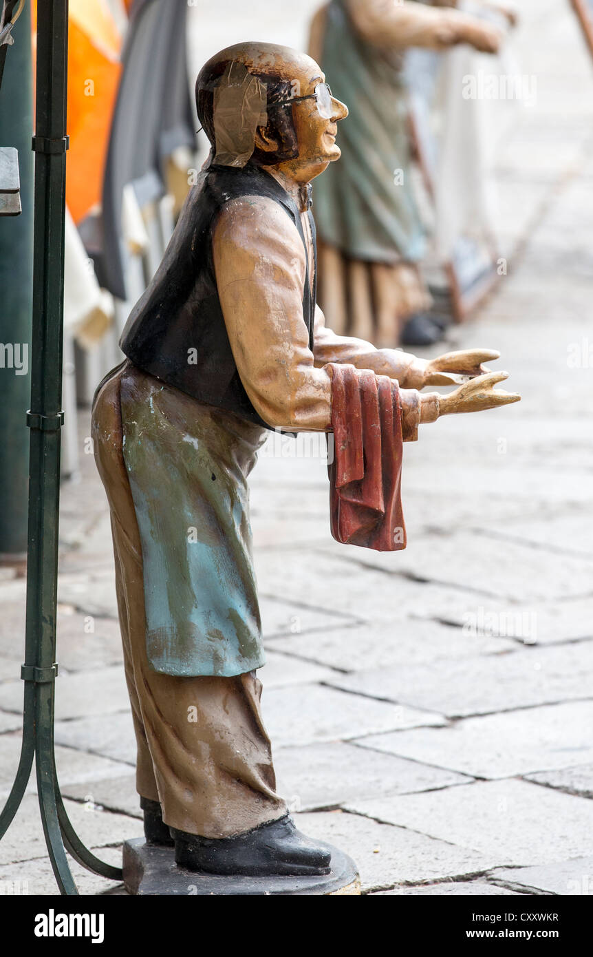 A plaster statuette of a waiter wearing an apron and holding a towel ...