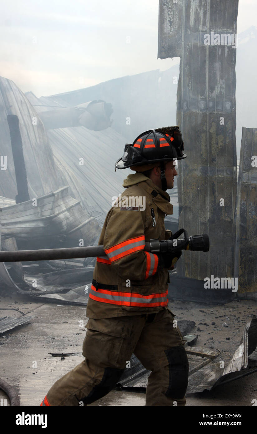 A firefighter carrying a hose at a fire scene Stock Photo - Alamy