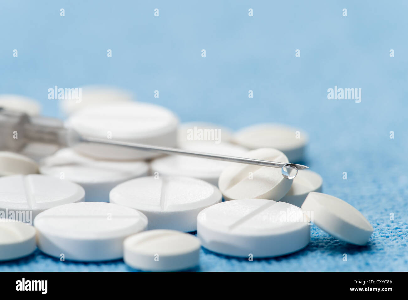 Hypodermic needle with drip medication spilled capsules on blue ...