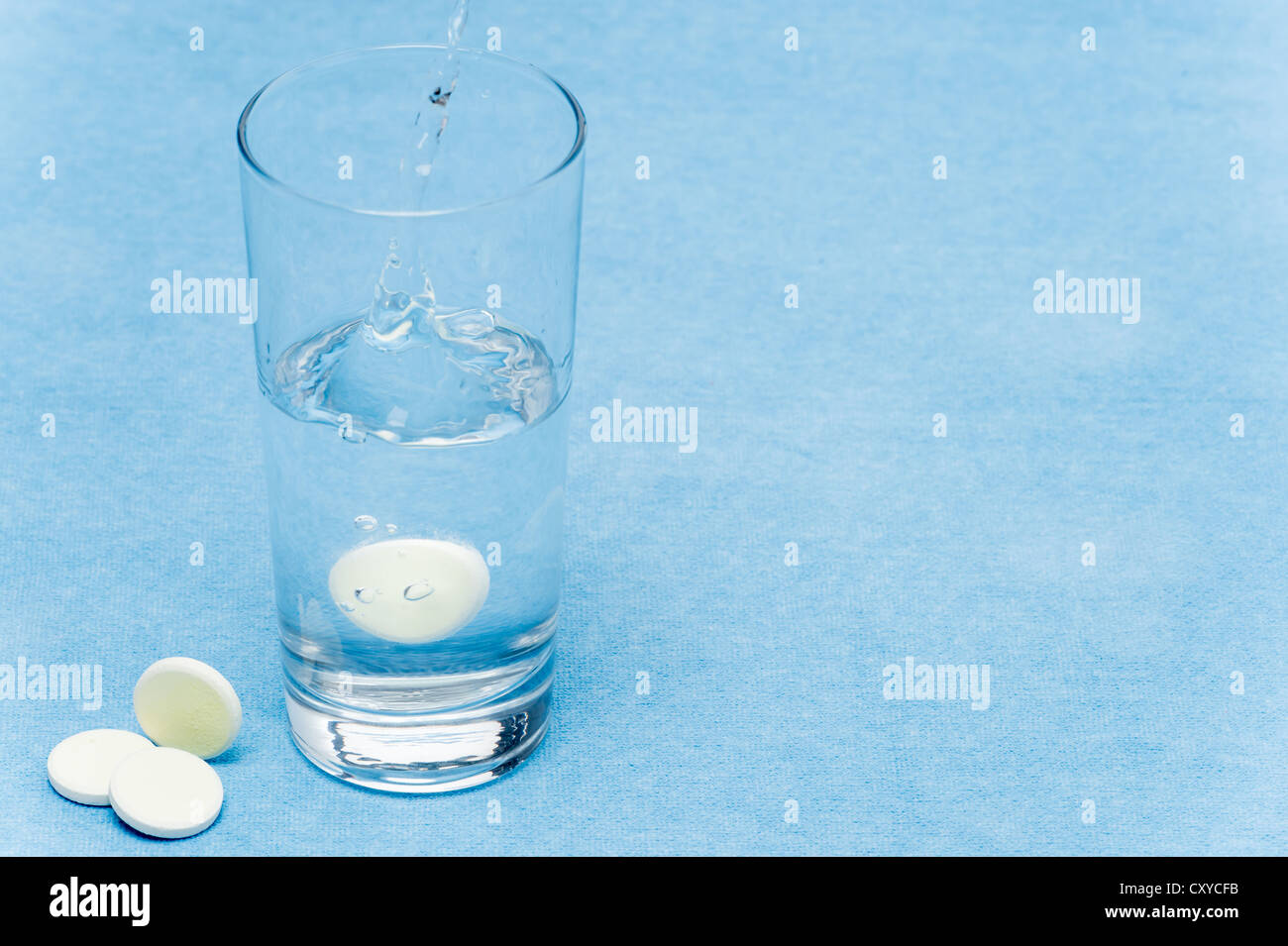 Soluble tablet throw in water glass on blue background Stock Photo - Alamy