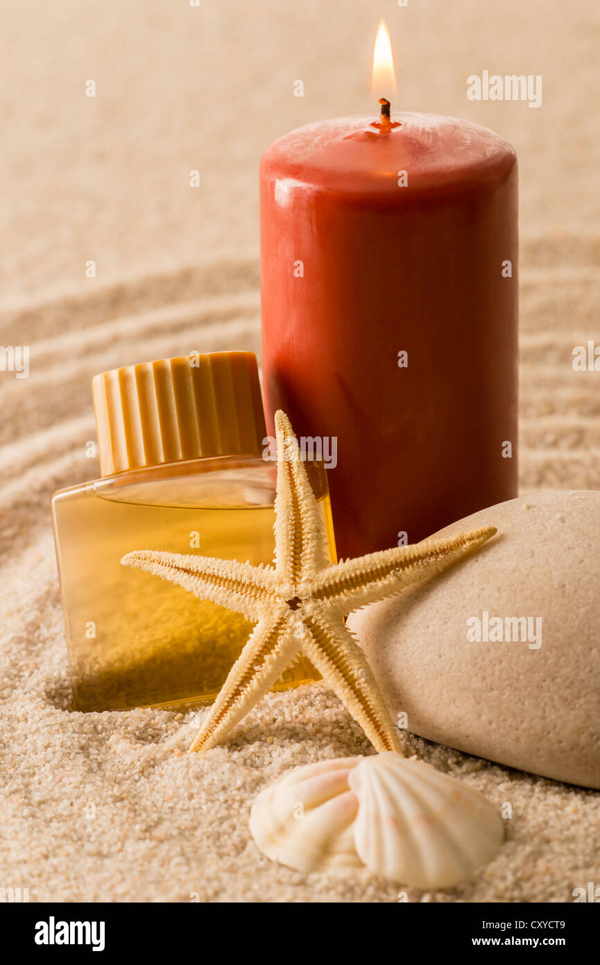 Spa setting candle with oil seashell star on sand Stock Photo - Alamy