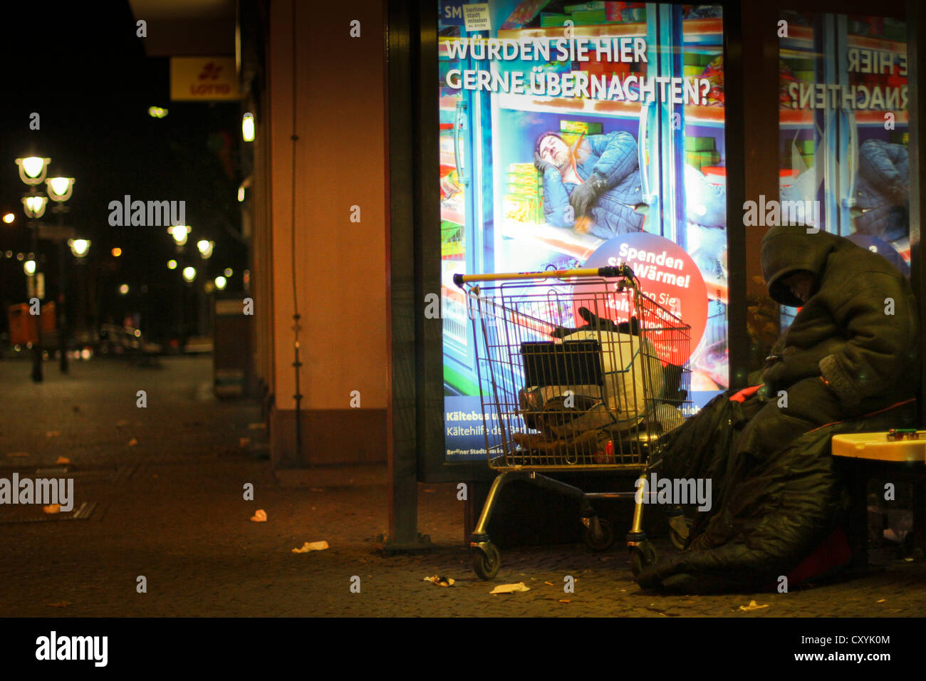 Man sleeping at a bus stop on a freezing cold winter's night in front ...