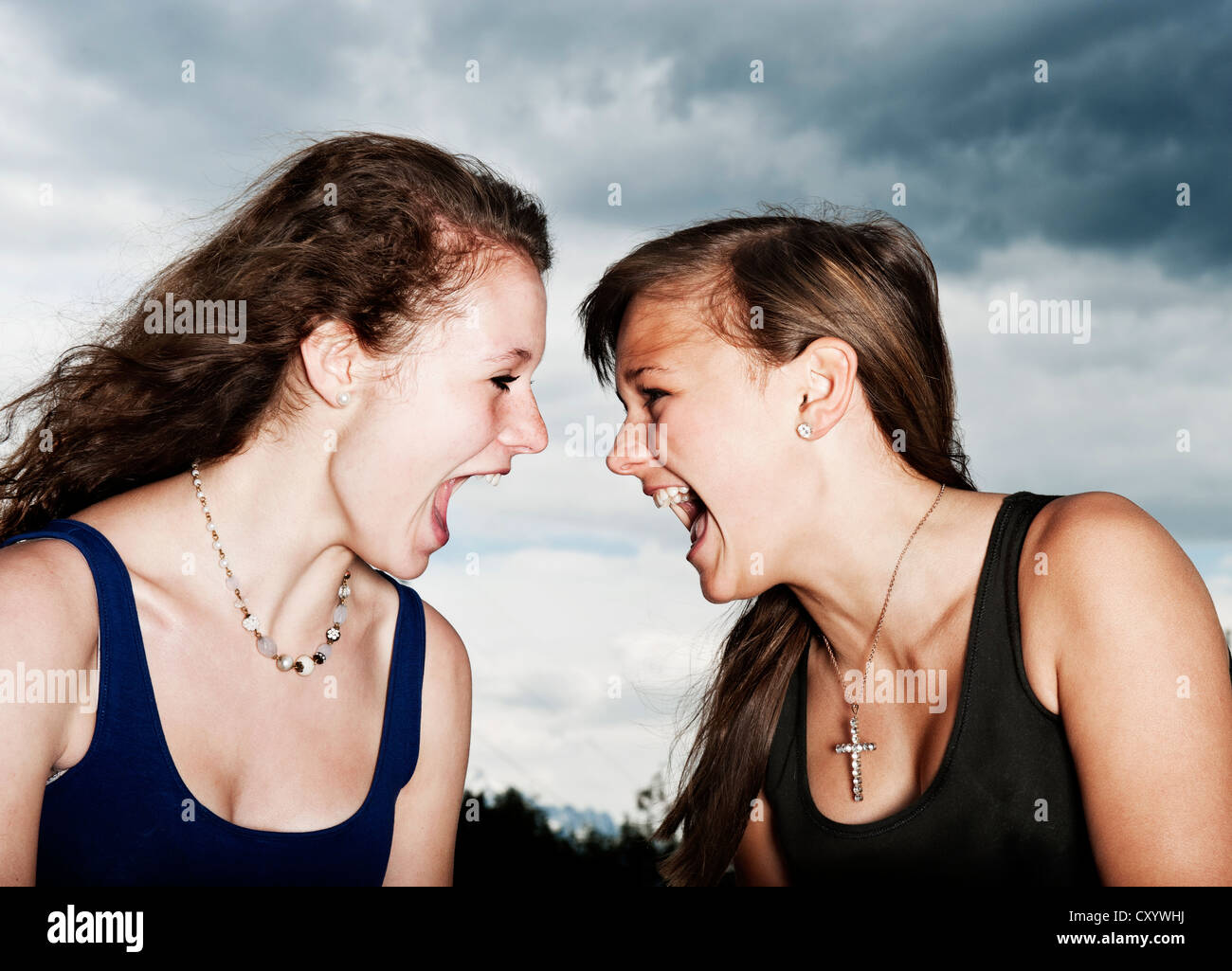 Two teenage girls screaming at each other, in front of storm clouds ...
