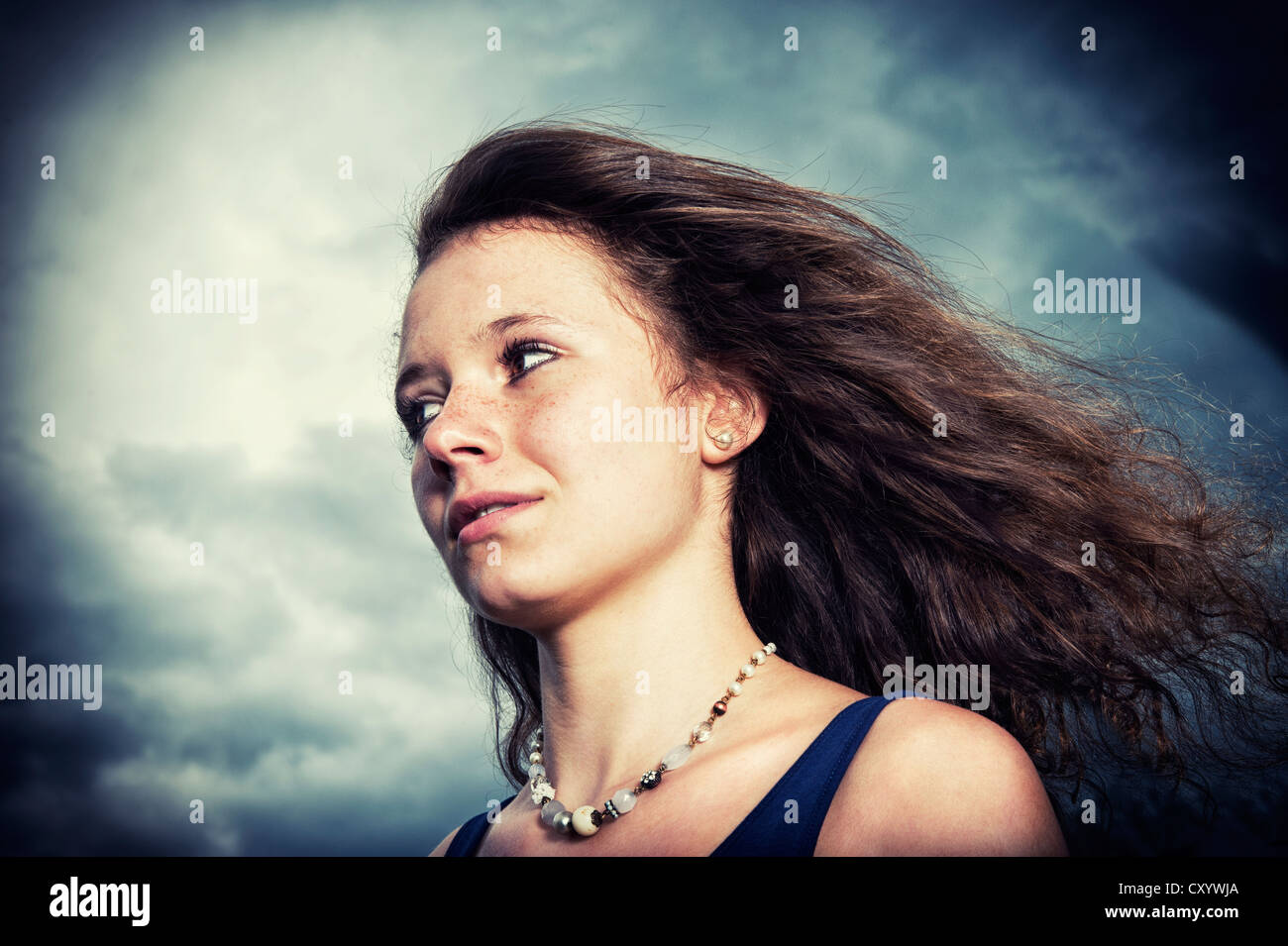 Girl, 14 years, with long hair in front of a gloomy cloudy sky ...
