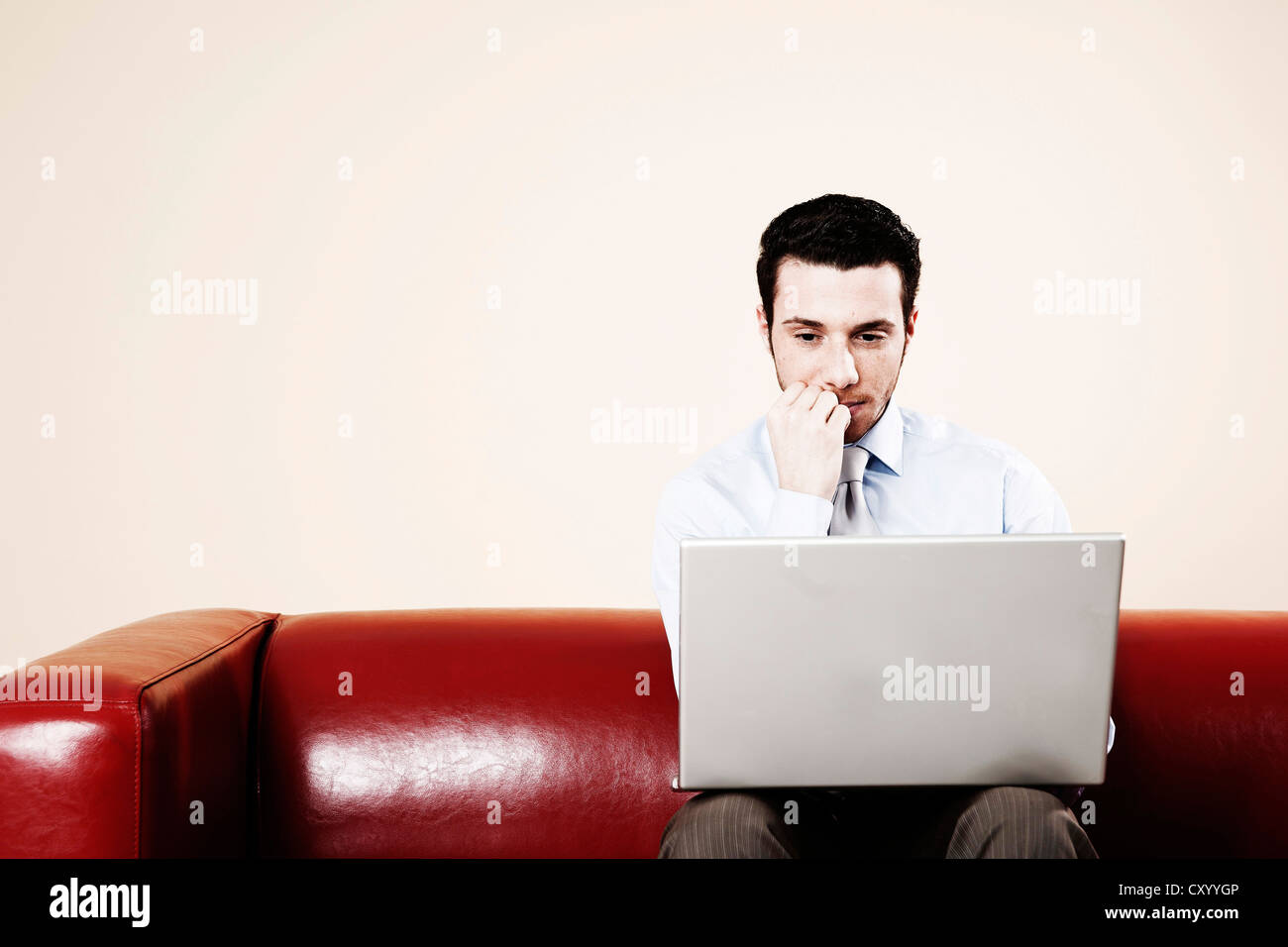 Young man sitting with his laptop computer on a sofa, thoughtful Stock ...