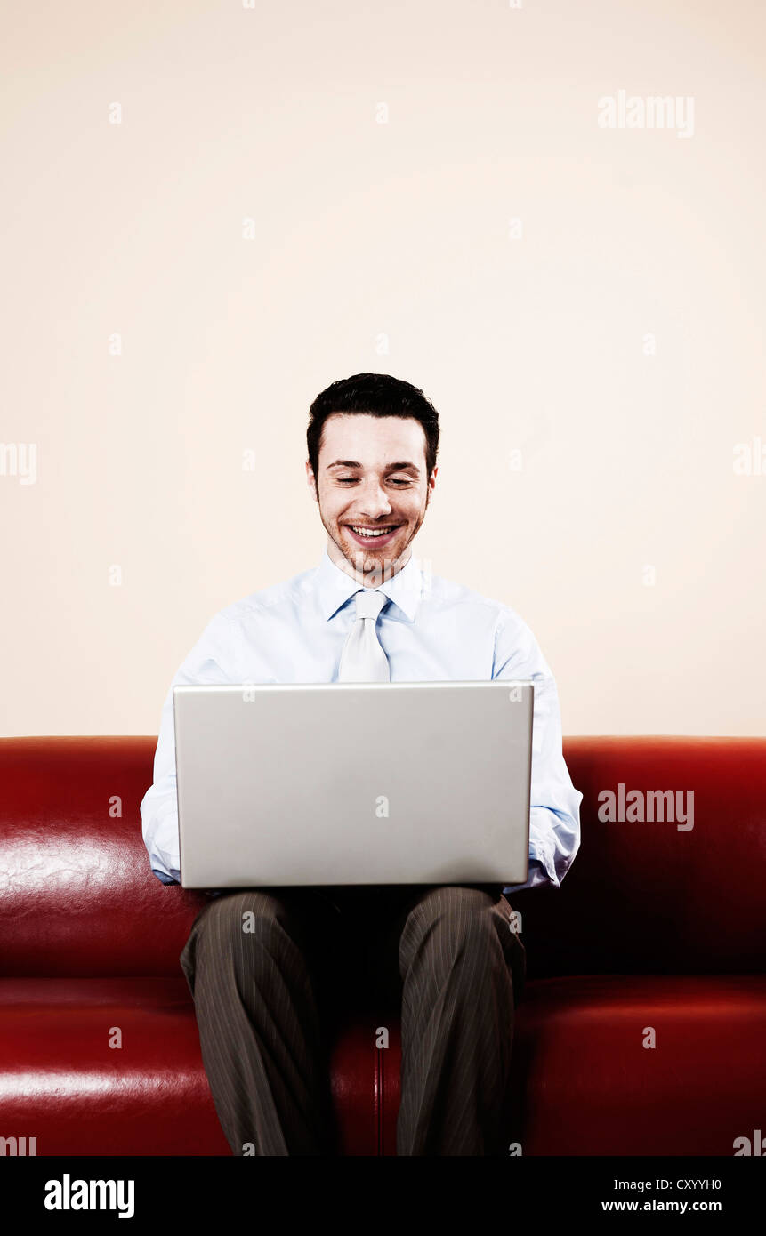 Young man sitting with his laptop computer on a sofa, cheerful Stock ...