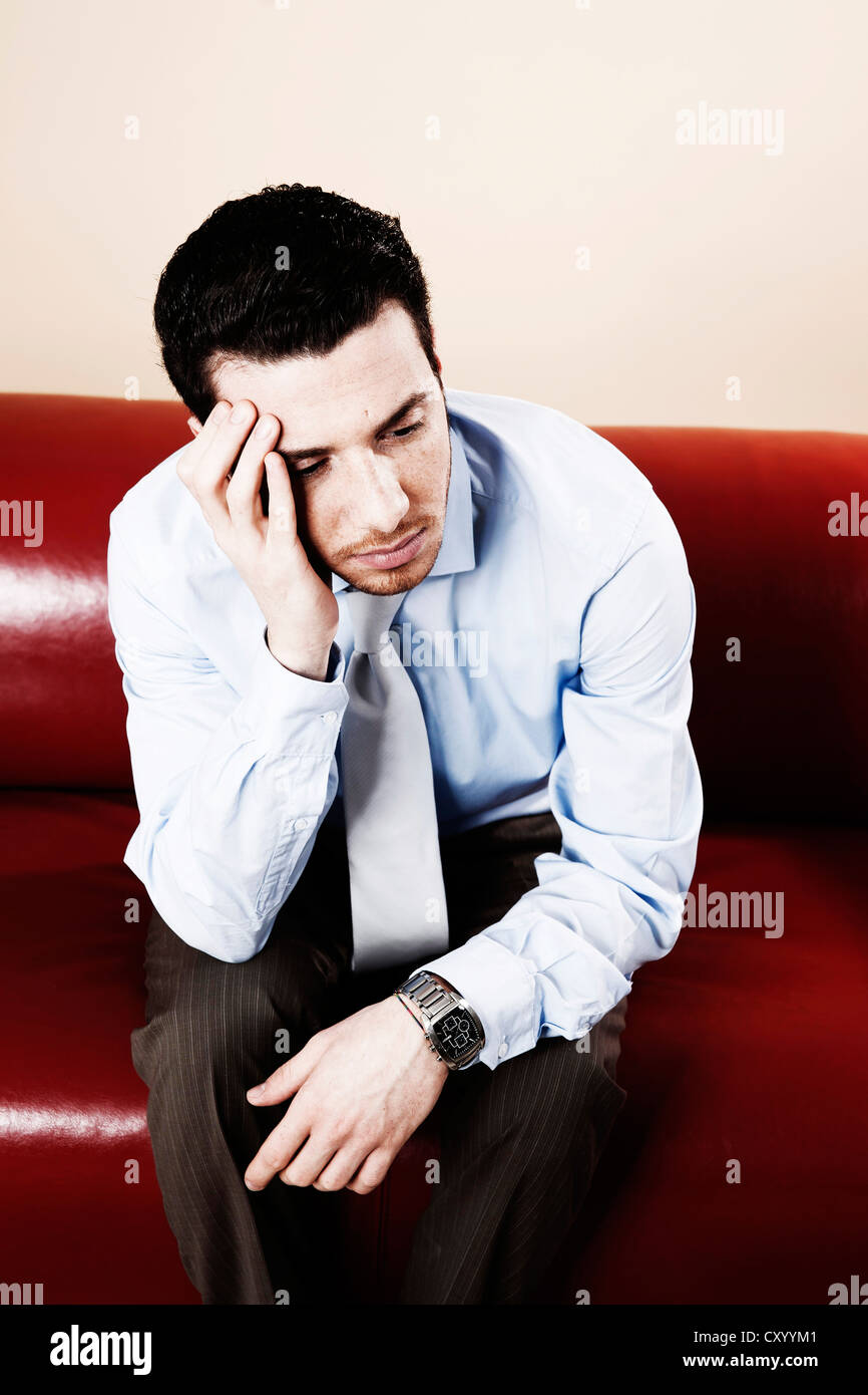 Young man sitting pensively on a sofa and waiting Stock Photo - Alamy