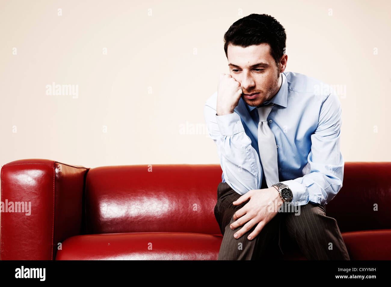 Young man sitting pensively on a sofa and waiting Stock Photo - Alamy
