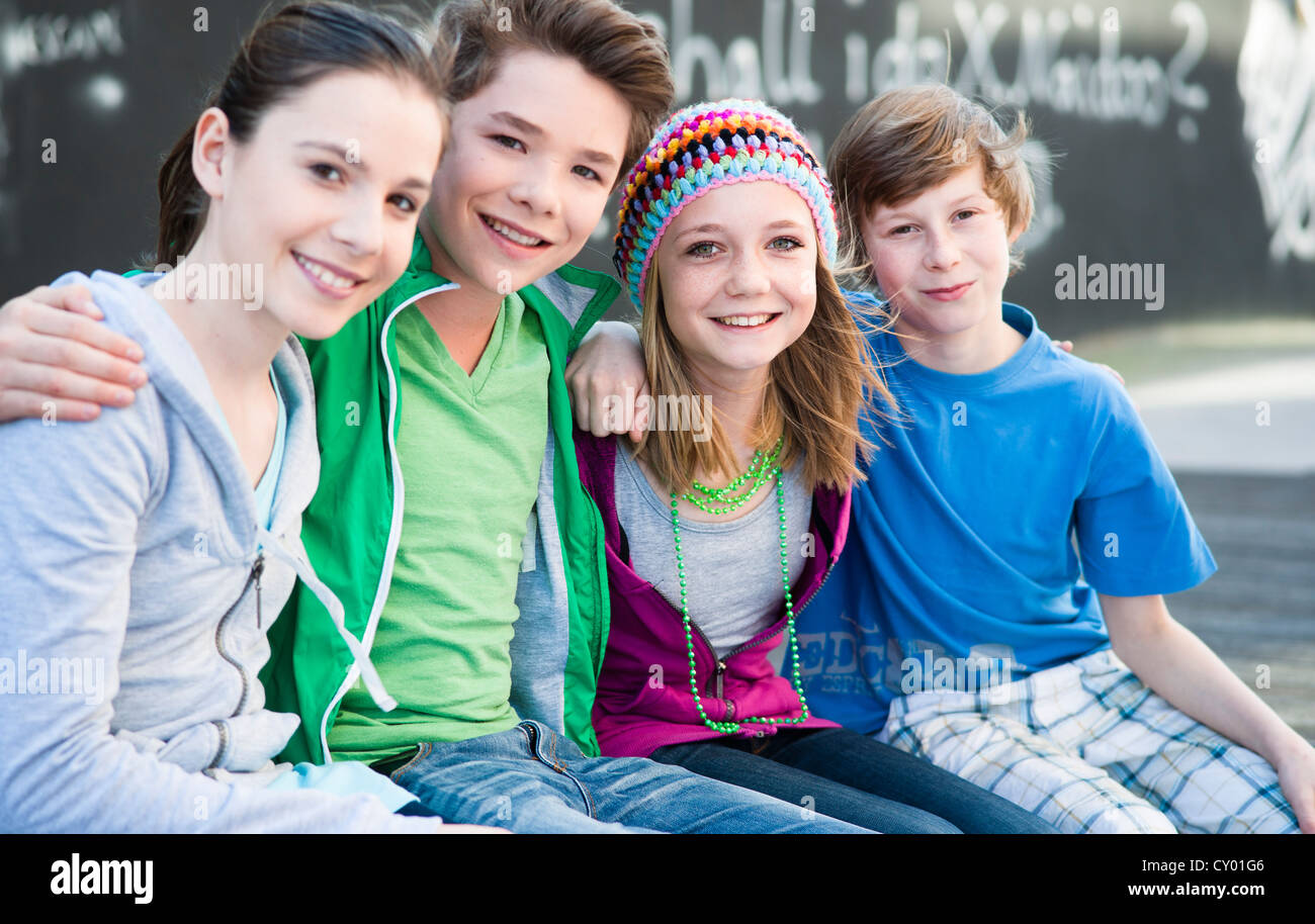 Four teenagers sitting in front of a wall with graffiti Stock Photo - Alamy